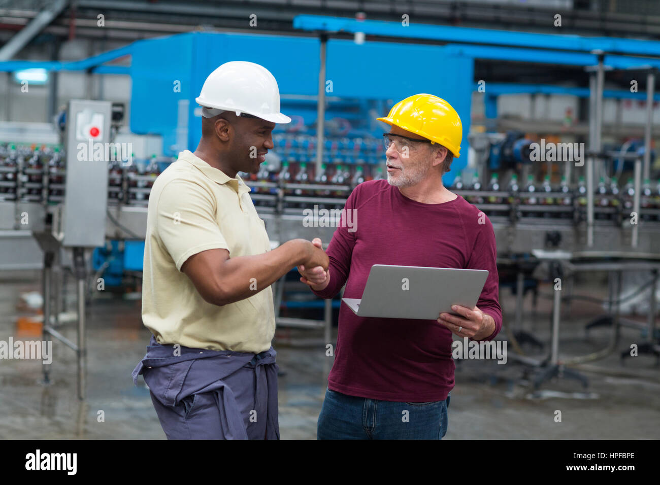 Factory workers with laptop shaking hands with his colleague in drinks ...
