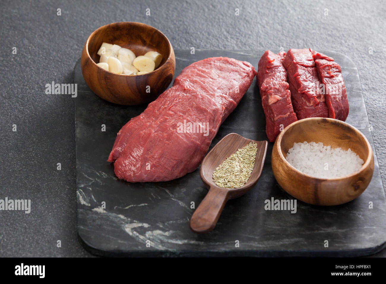 Beef steak, salt and spices on black slate plate against black ...