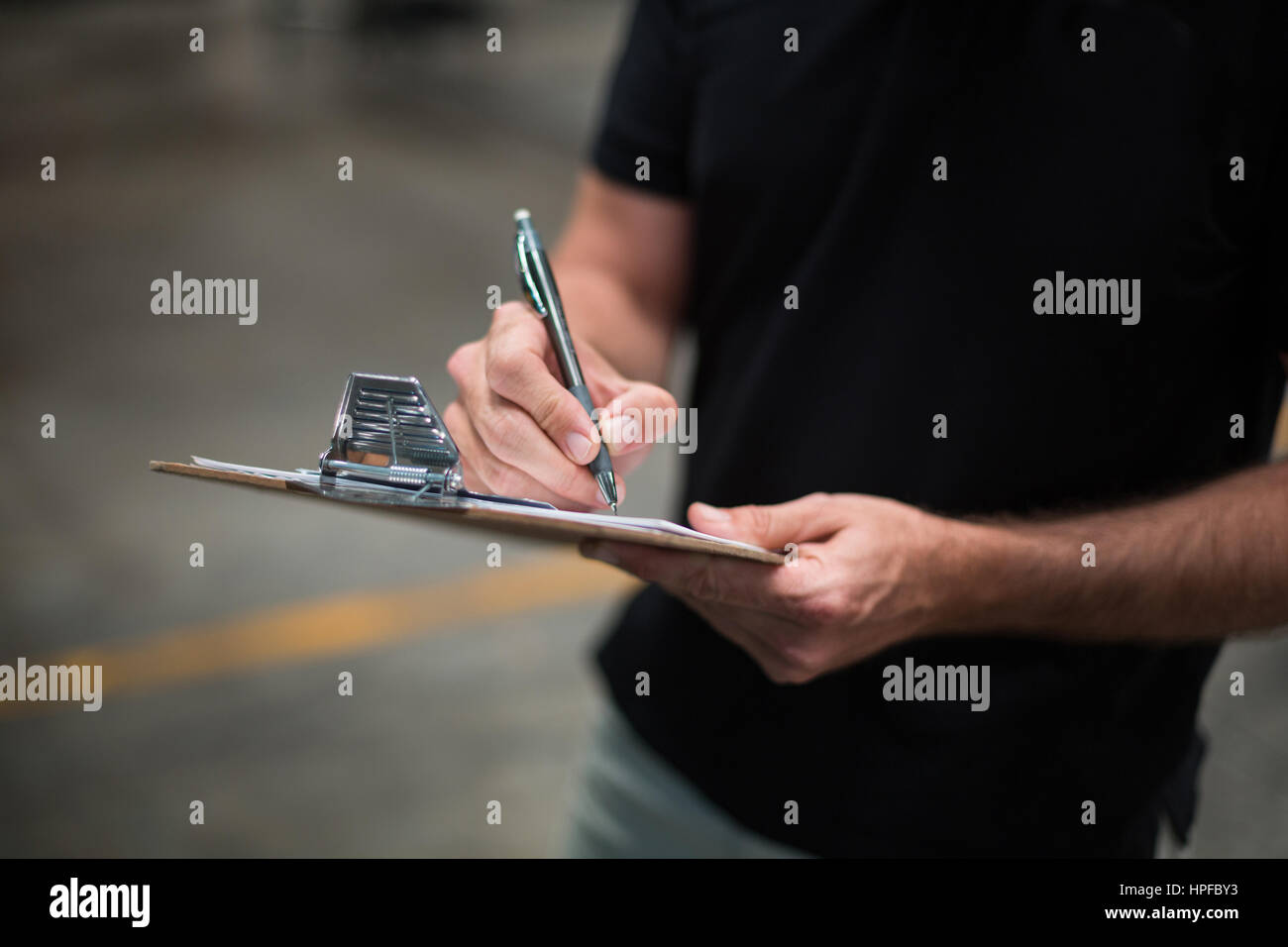 Mid section of factory staff writing on clipboard in factory Stock ...