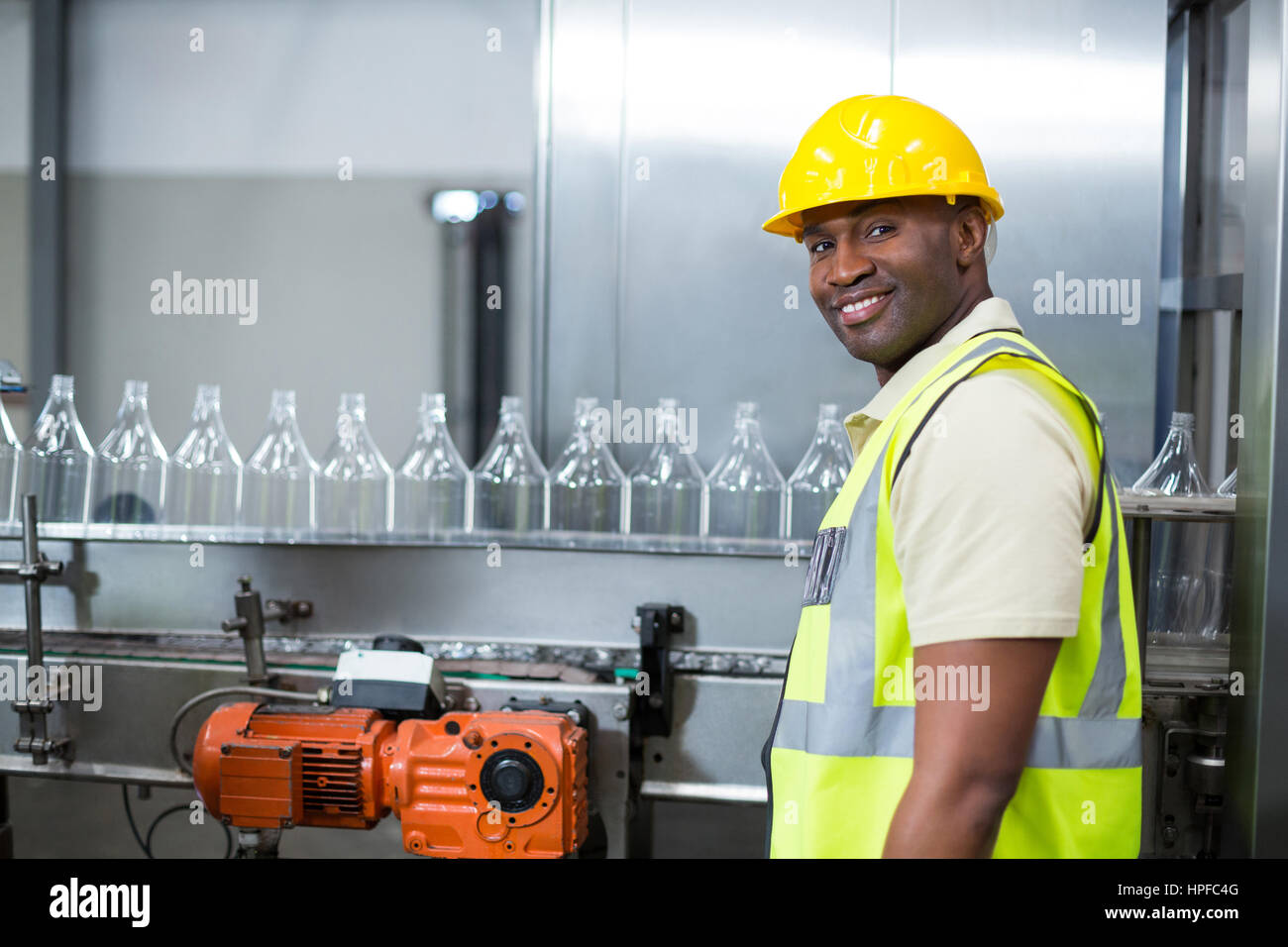 Smiling factory worker standing next to production line at drinks ...