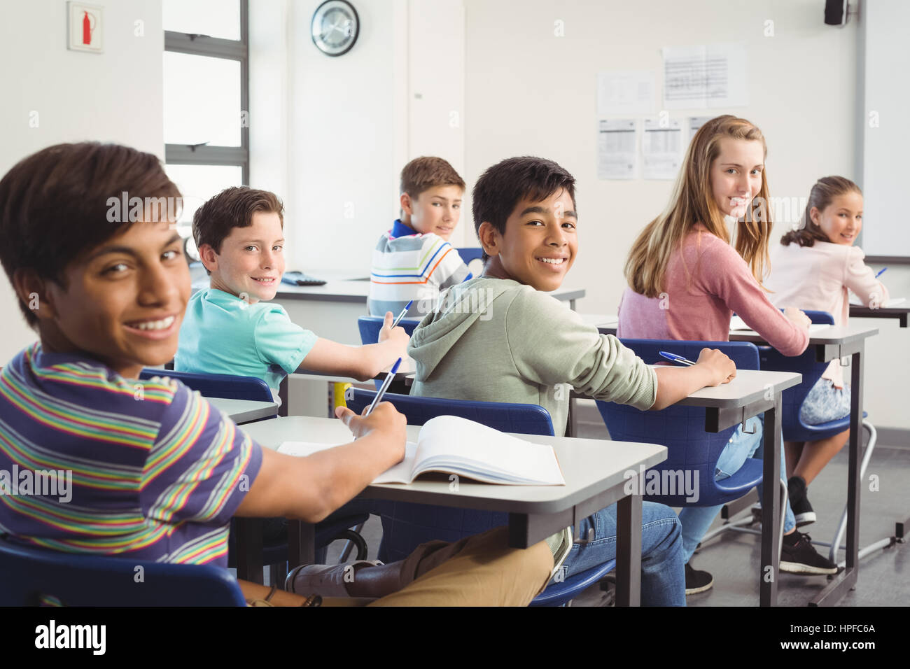 Portrait of smiling school kids doing homework in classroom at school ...