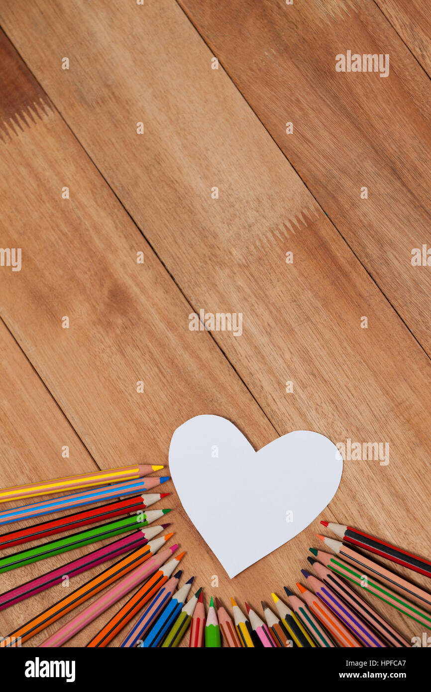Colored pencil arranged around heart shape paper on wooden background ...