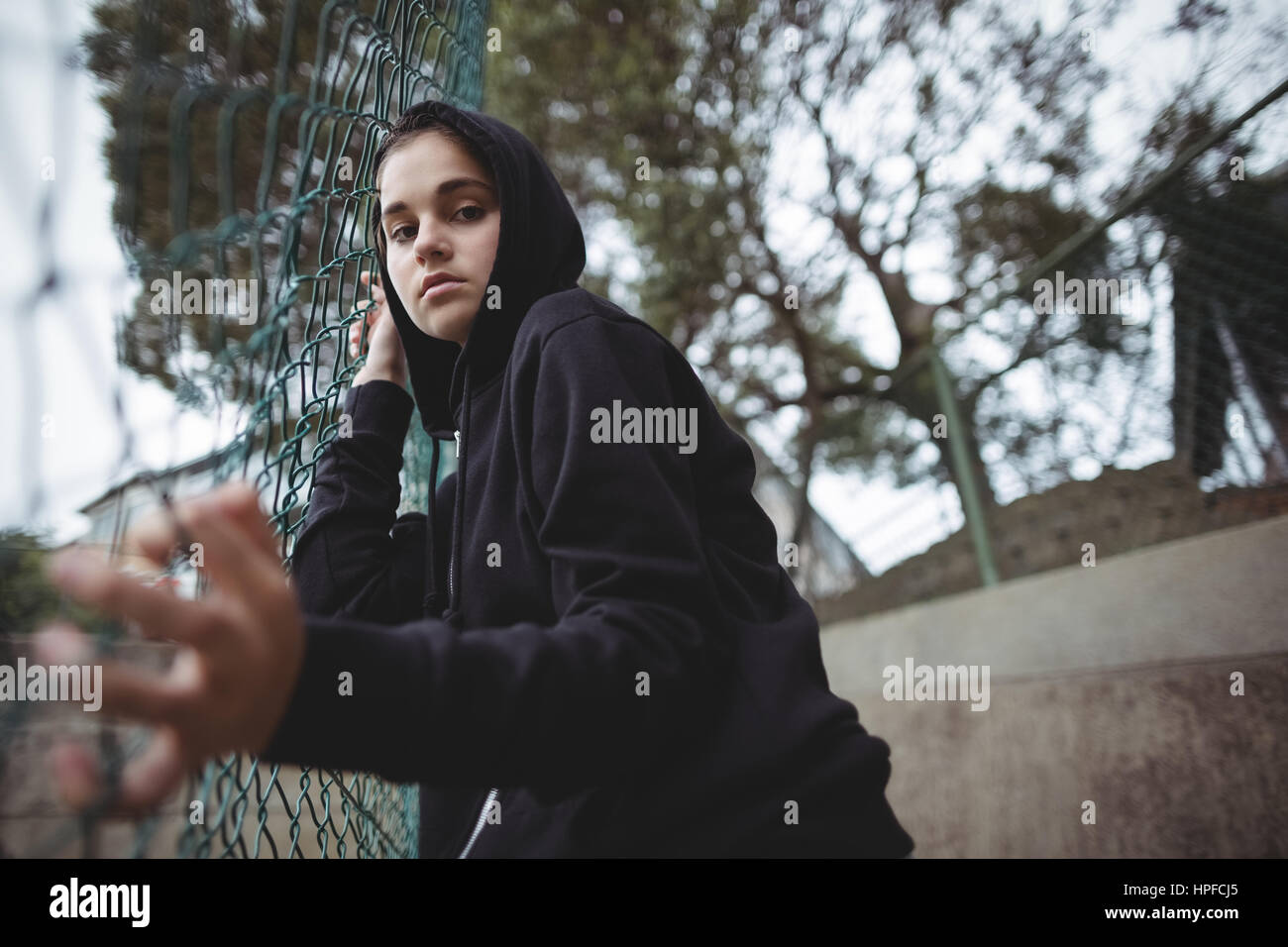 Portrait of anxious teenage girl leaning on wire mesh fence at school ...