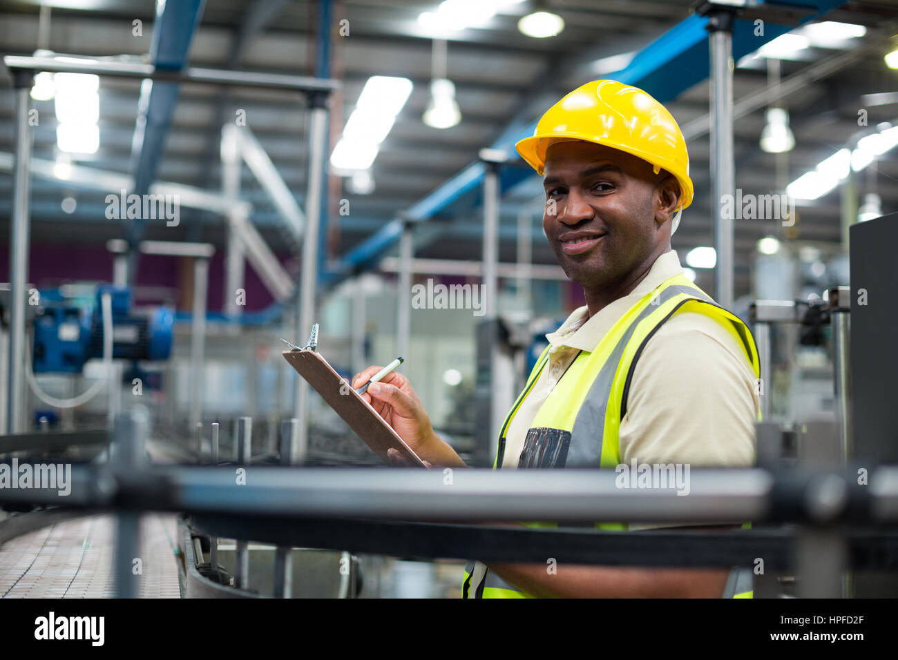 Portrait of smiling factory worker writing on clipboard in factory ...
