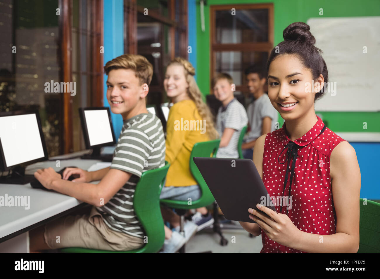 Smiling students studying on digital tablet and computer in classroom ...