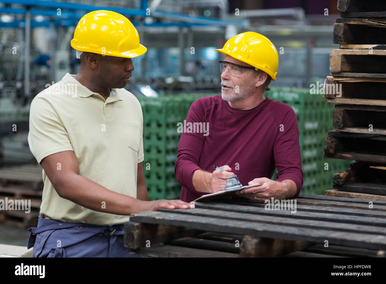 Two factory workers discussing with a clipboard in drinks production ...