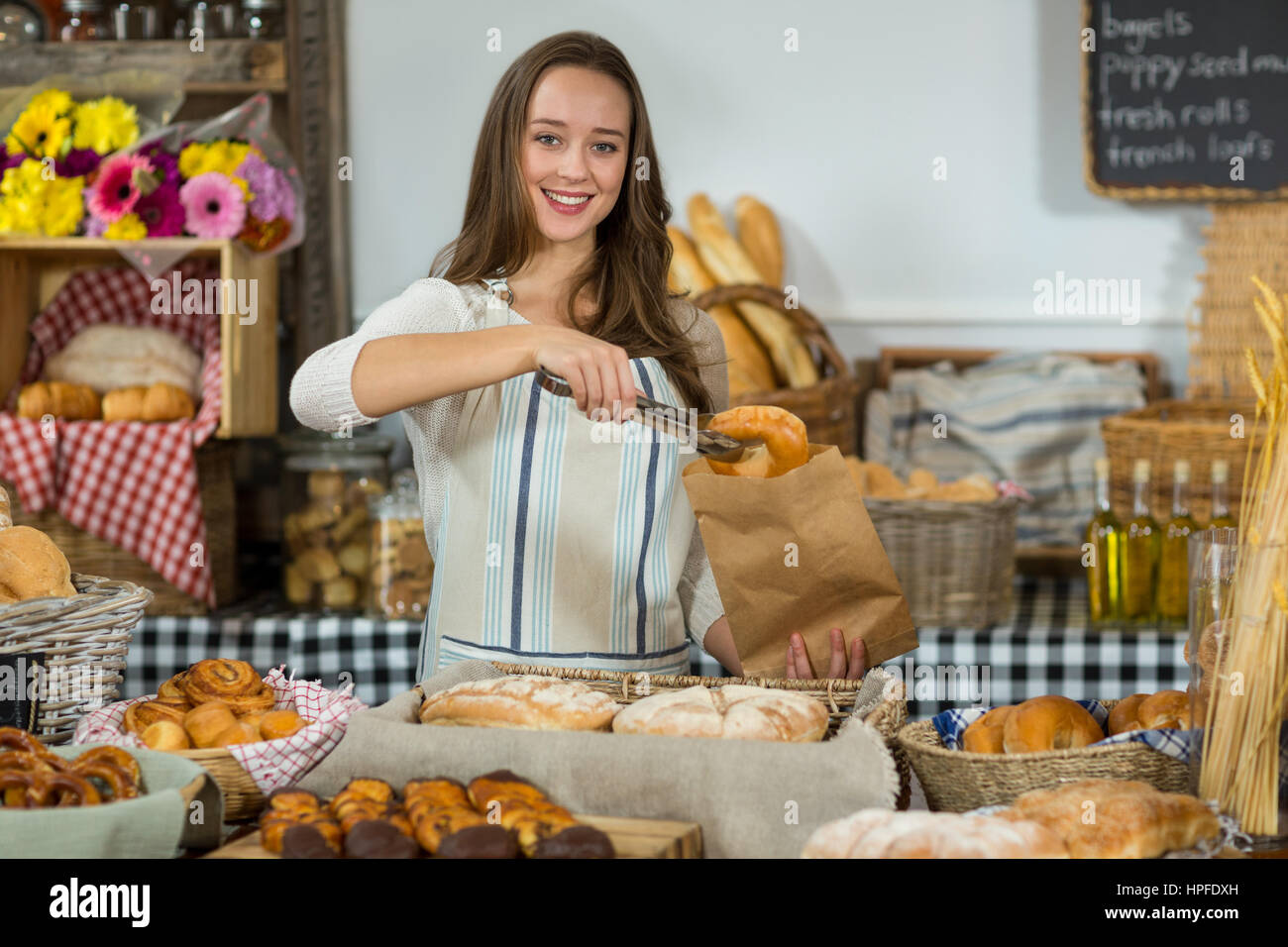 Portrait of smiling female staff putting croissant into a paper bag at ...