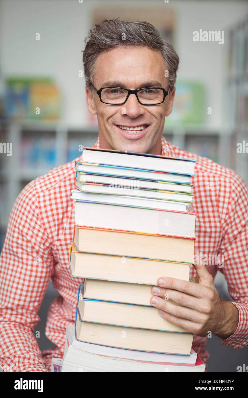 Portrait of school teacher holding stack of books in library at school ...