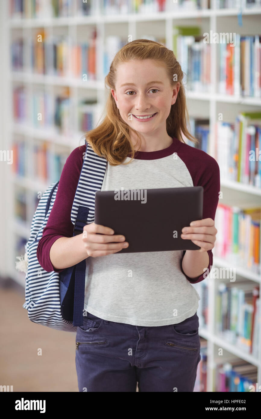 Portrait of happy schoolgirl holding digital tablet in library at ...