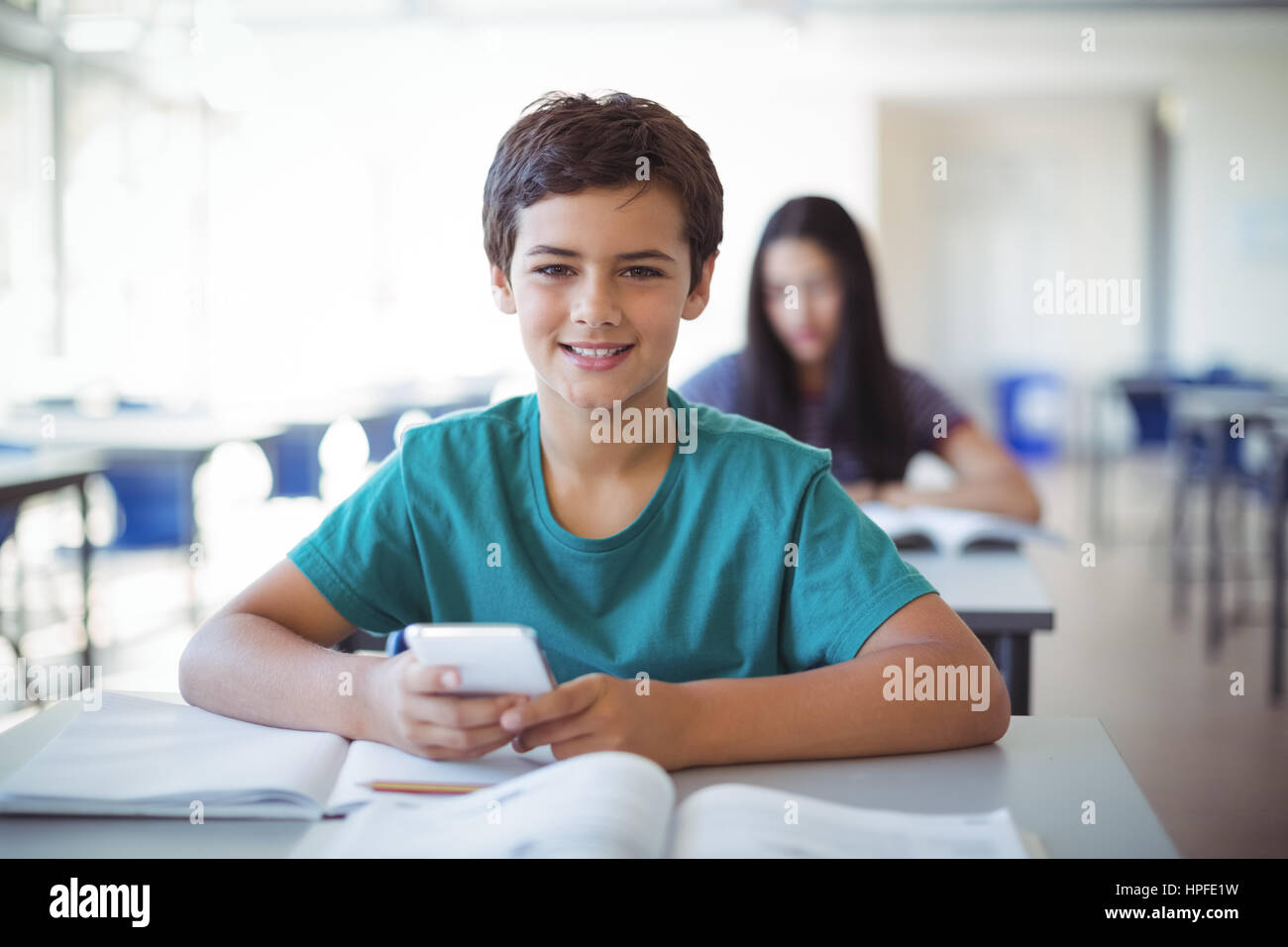 Portrait of schoolboy using mobile phone while studying in classroom at ...
