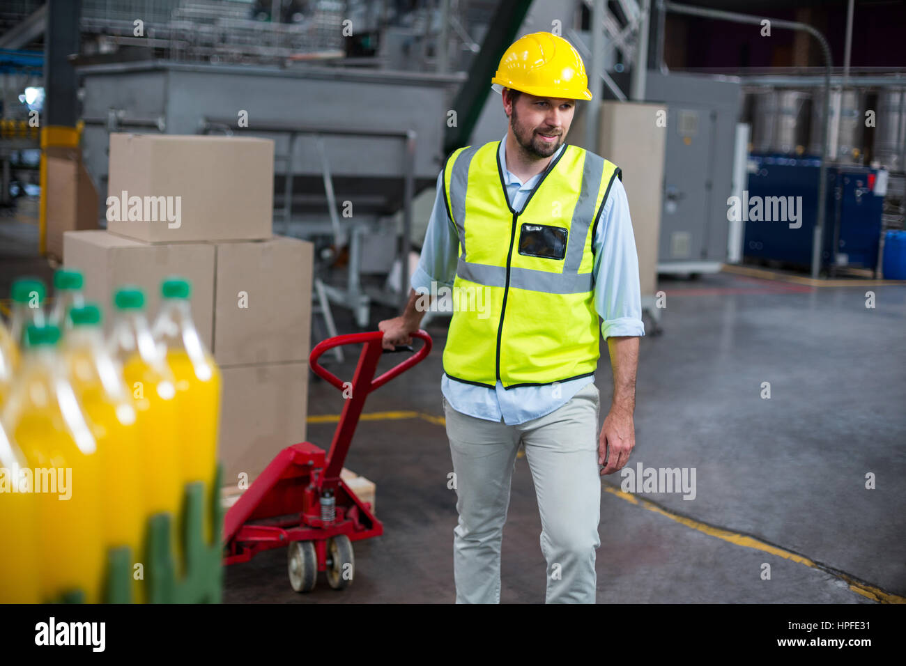 Factory worker pulling trolley of cardboard boxes in factory Stock ...