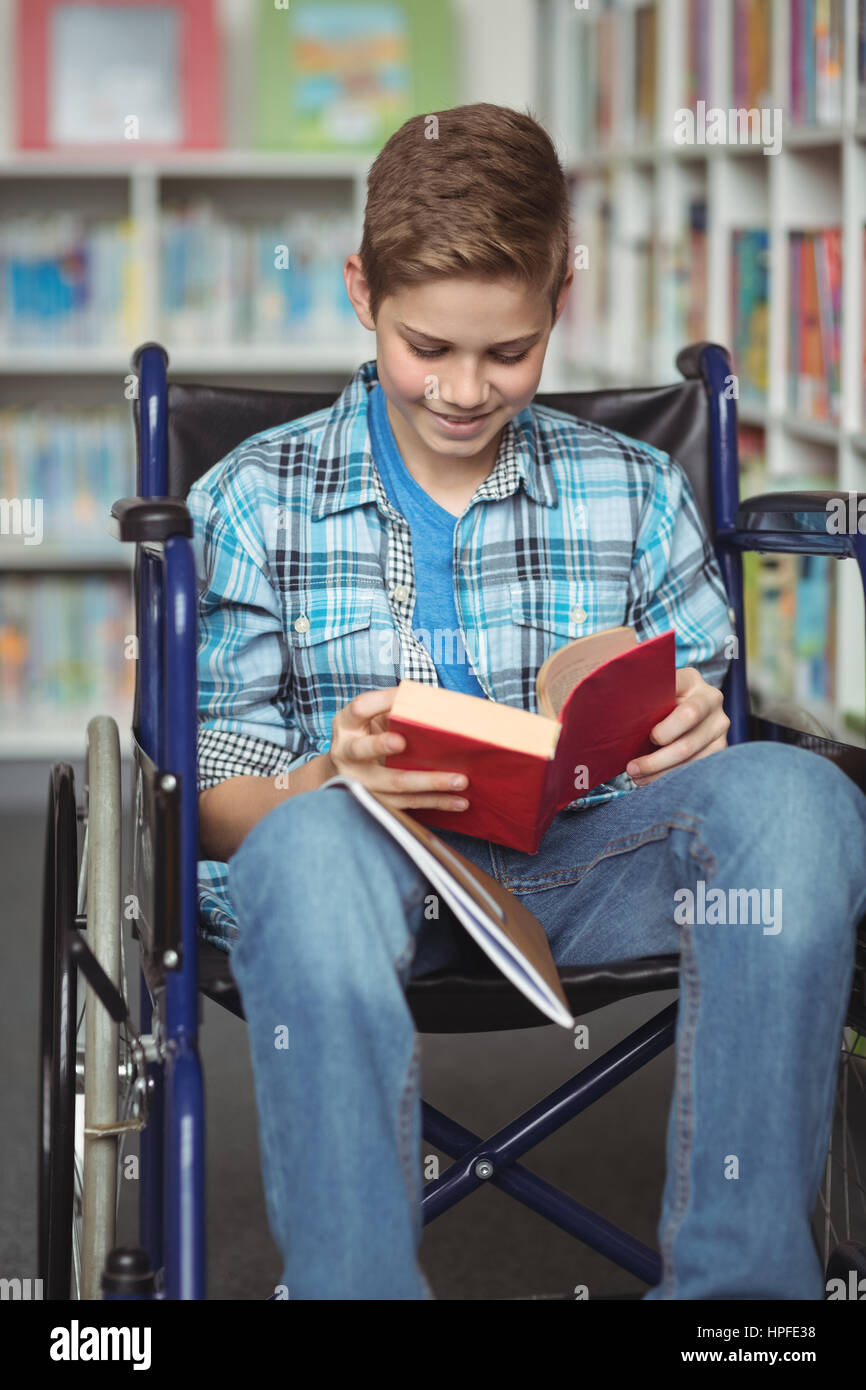 Disabled schoolboy reading book in library at school Stock Photo - Alamy