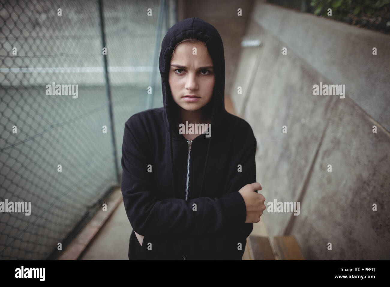 Portrait of anxious teenage girl standing with arms crossed at school ...