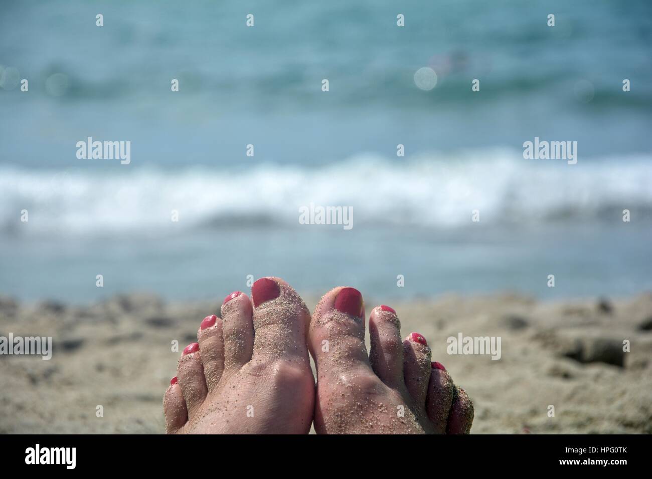 Sandy feet with red toenails on the beach with blurred sea in the ...