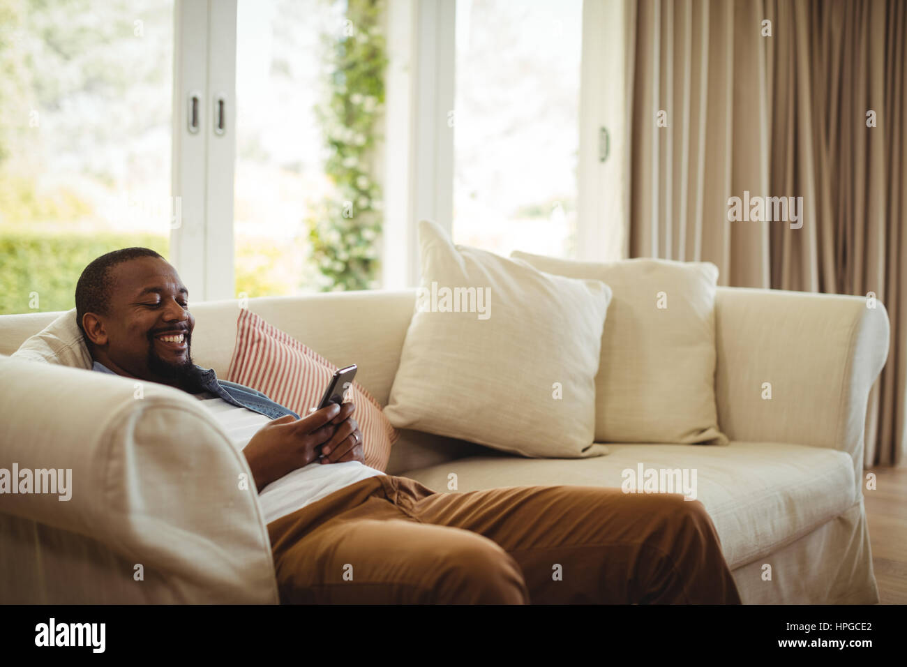 Man sitting on sofa and using mobile phone in living room at home Stock ...
