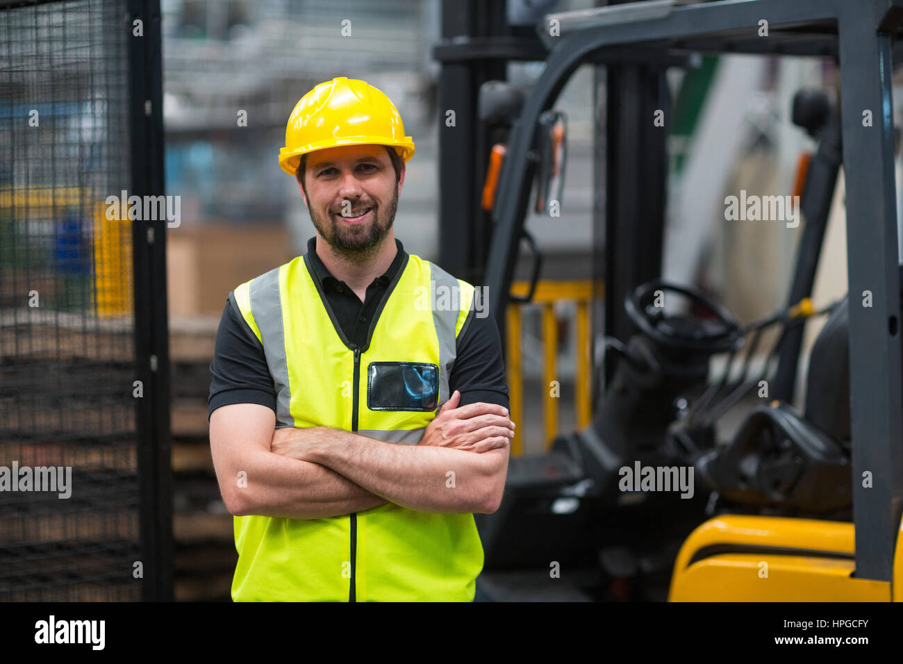 Portrait of smiling factory worker standing with arms crossed in ...