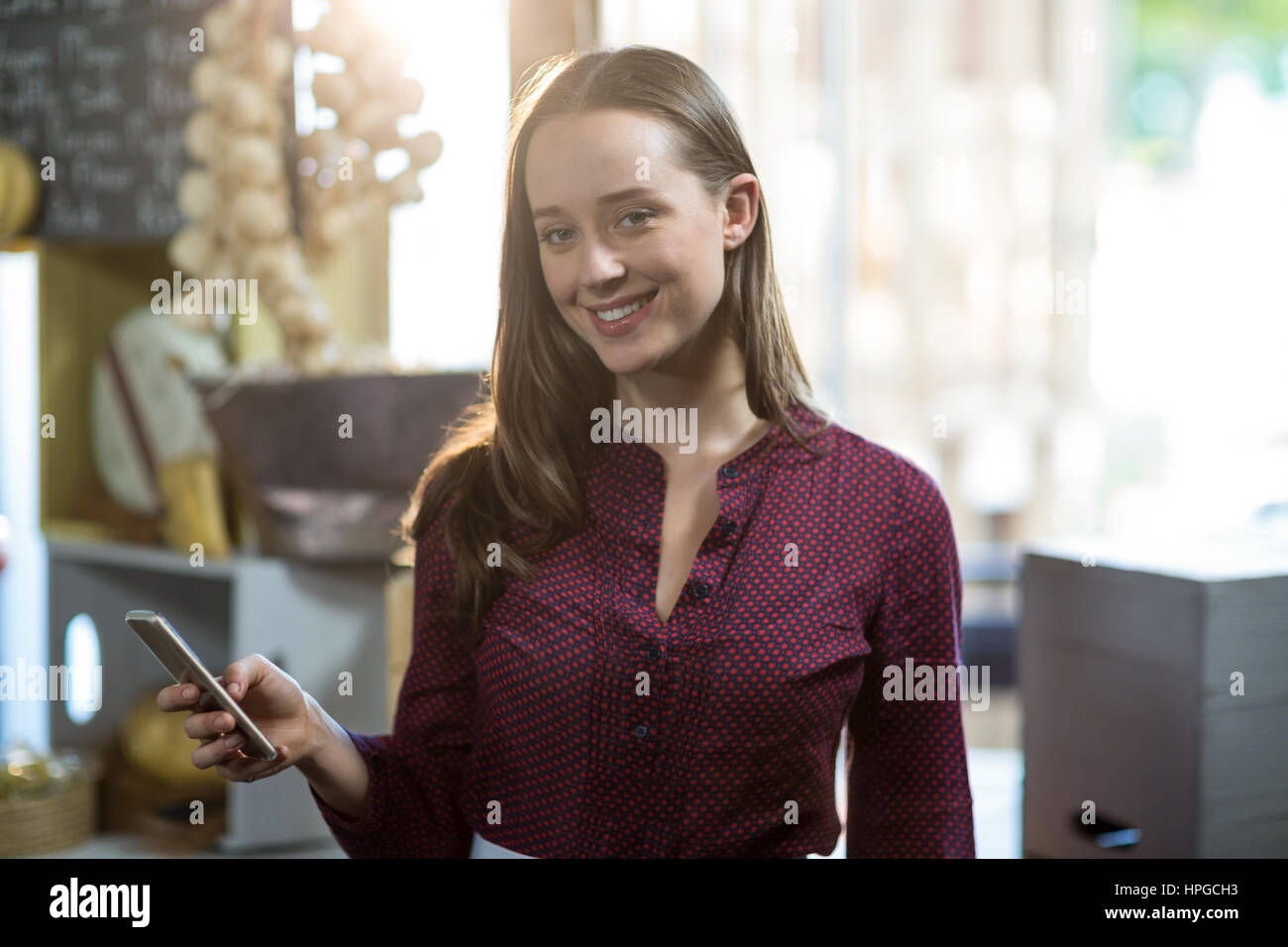 Portrait of smiling female staff using mobile phone at counter in bake ...