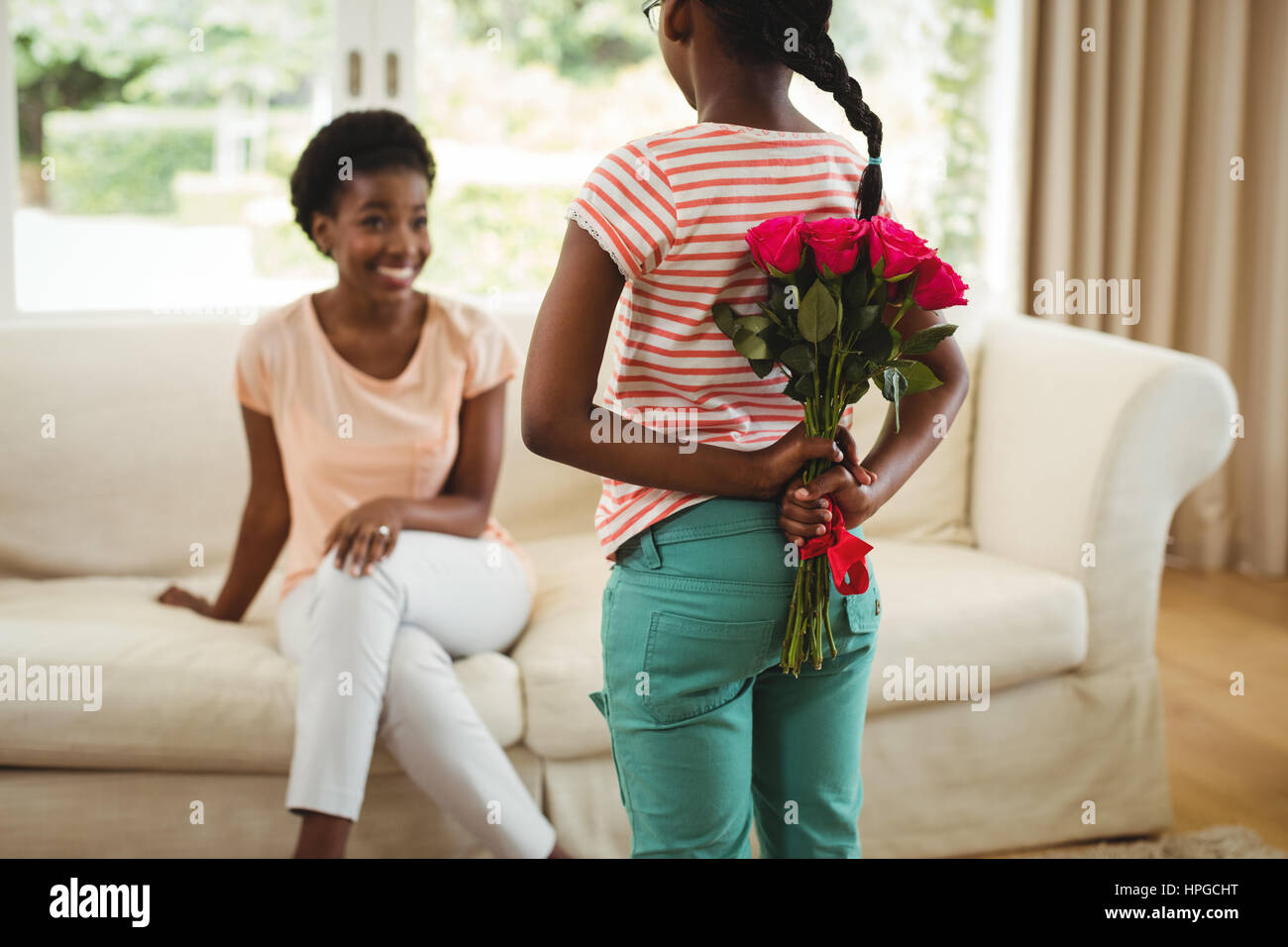 Daughter hiding flowers behind her back for mother at home Stock Photo ...