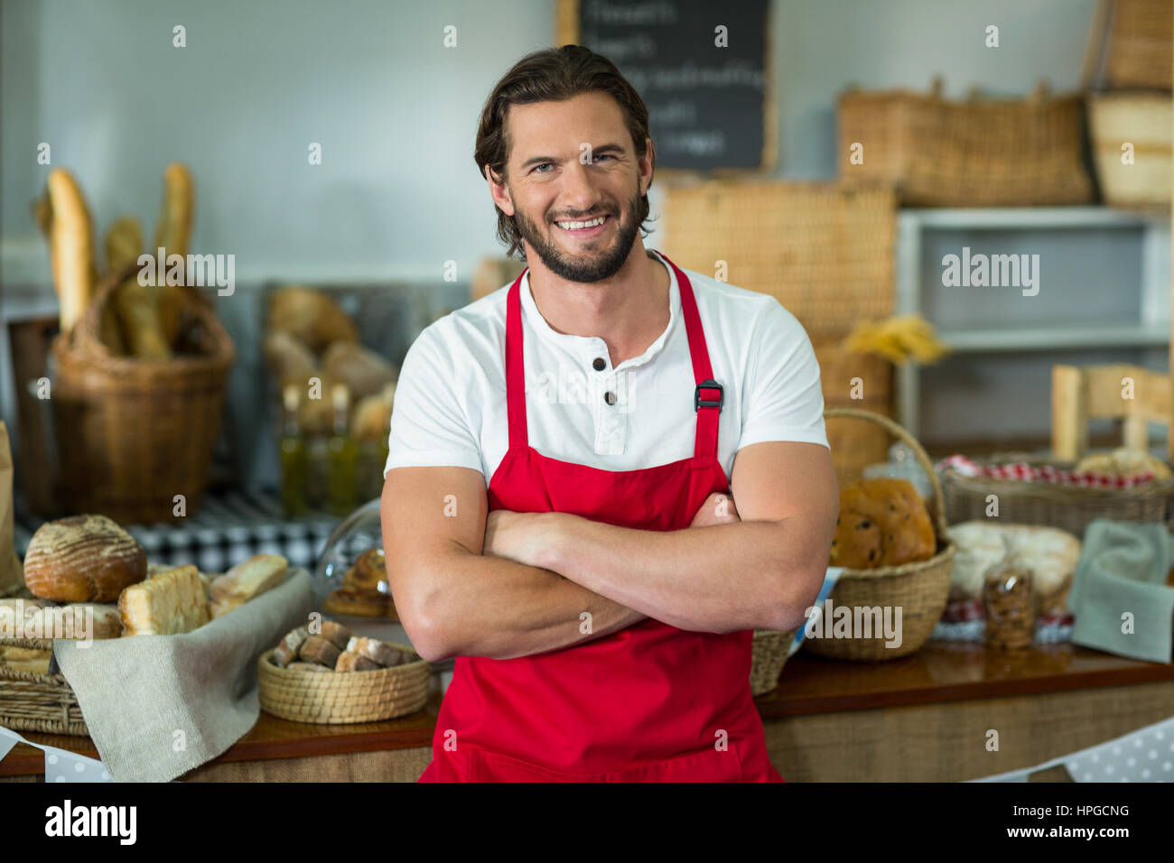 Portrait of smiling bakery staff standing with arms crossed at counter ...
