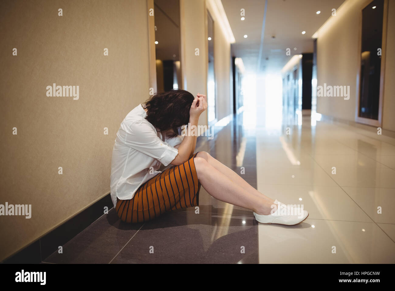 Sad female business executive sitting in corridor of office Stock Photo ...