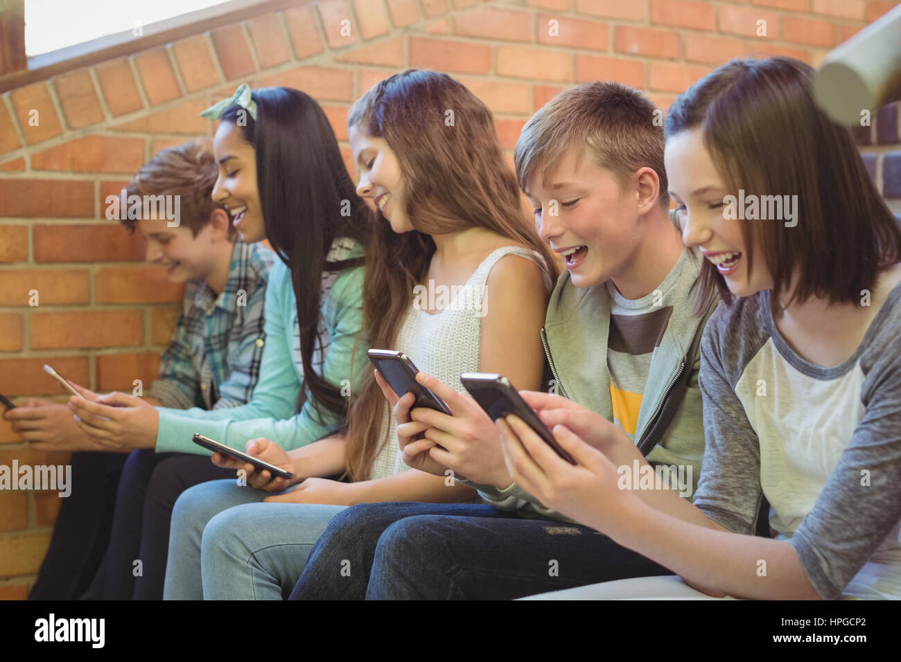 Group of smiling school friends sitting on staircase using mobile phone ...
