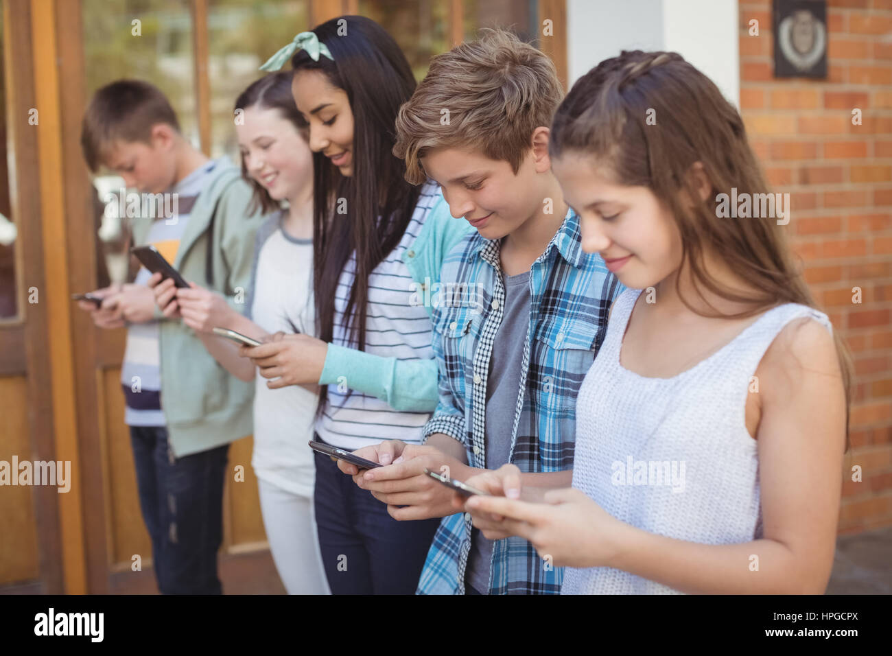 Group of smiling school friends using mobile phone in corridor at ...
