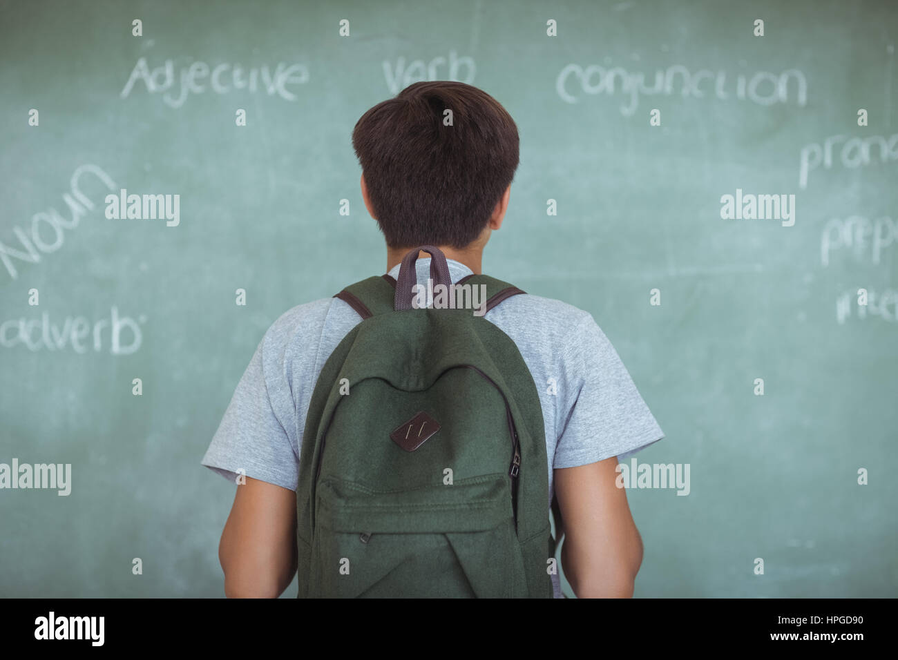 Rear view of schoolboy with backpack reading chalkboard in classroom at ...