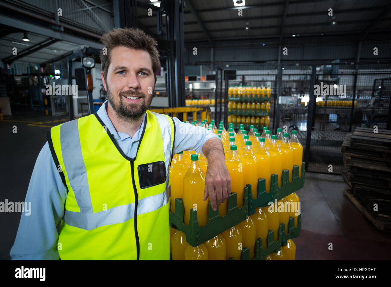Portrait of factory worker leaning on packed orange juice bottles crate ...