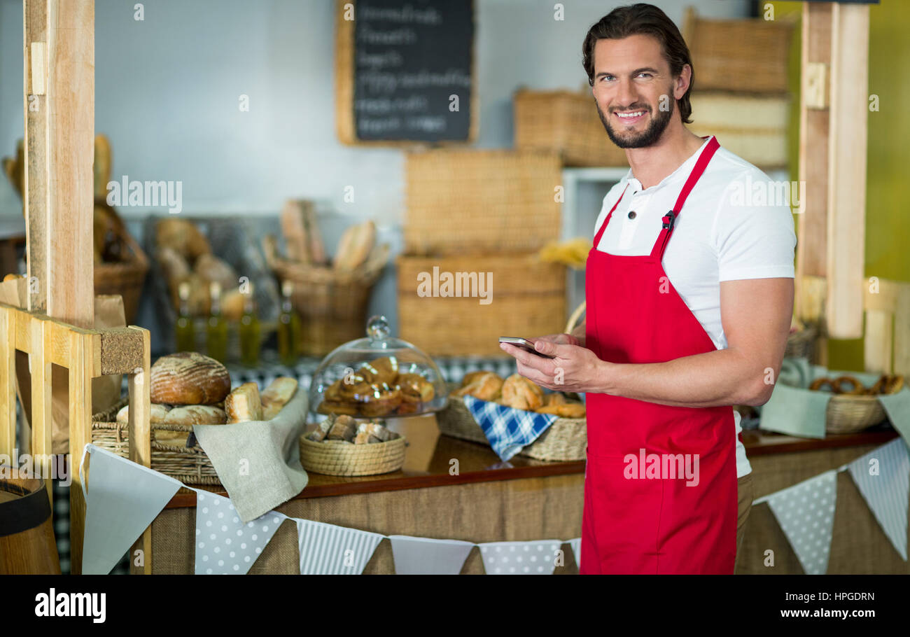 Portrait of smiling bakery staff using mobile phone at counter in bake ...
