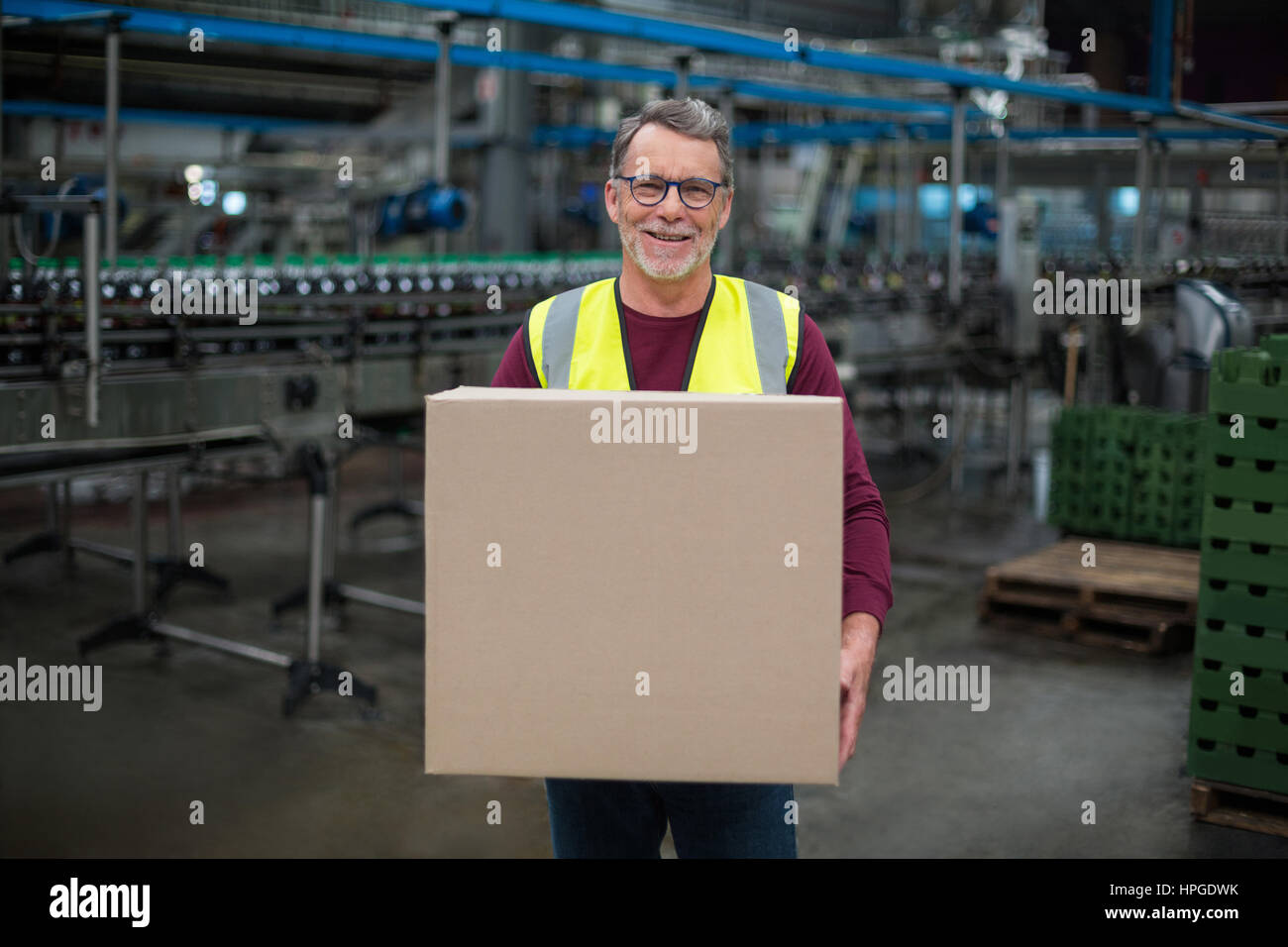 Portrait of factory worker holding cardboard box in drinks production ...