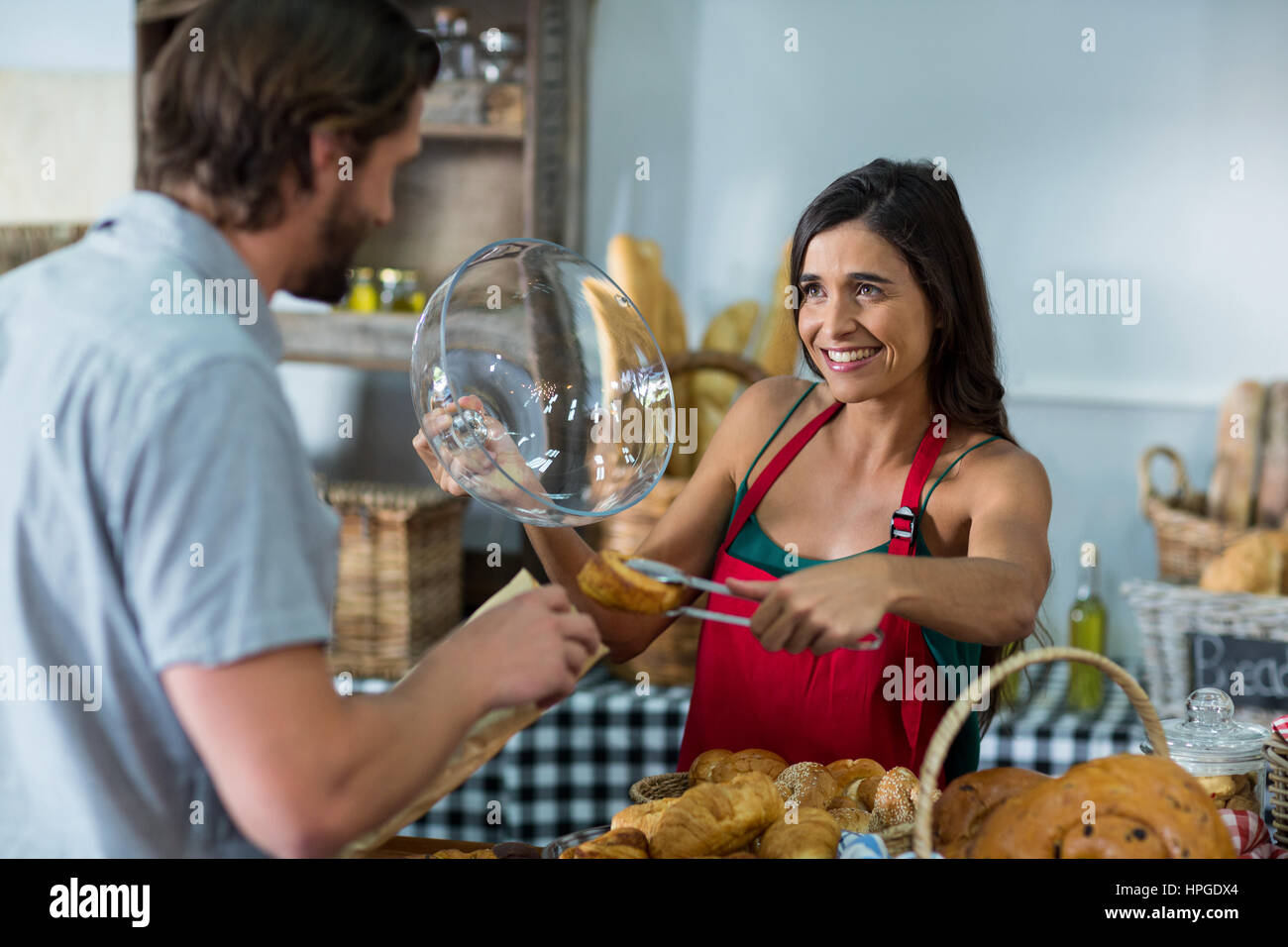 Bakery staff giving parcel to male customer at counter in bake shop ...