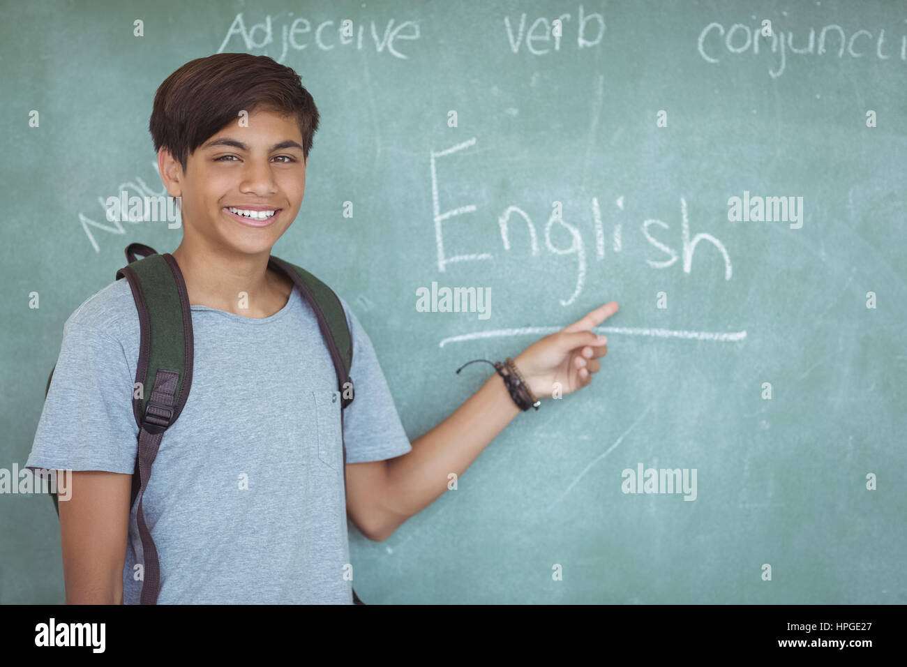 Portrait of happy schoolboy pointing at chalkboard in classroom at ...