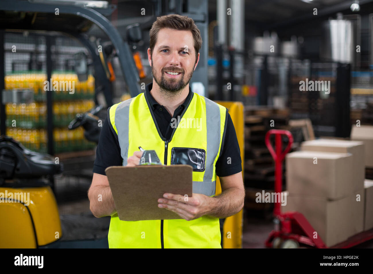 Smiling factory worker writing on clipboard in factory Stock Photo - Alamy