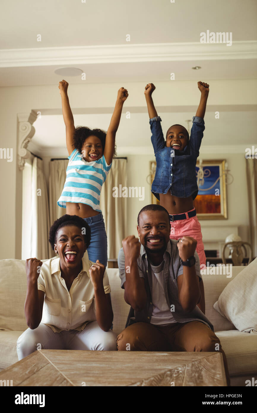 Parents and kids having fun while watching television in living room at ...