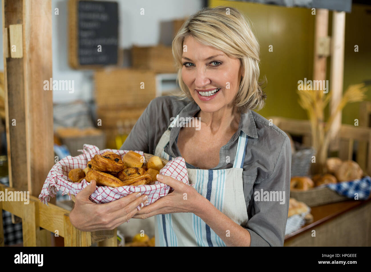 Portrait of smiling female staff holding a basket of baked snacks at ...