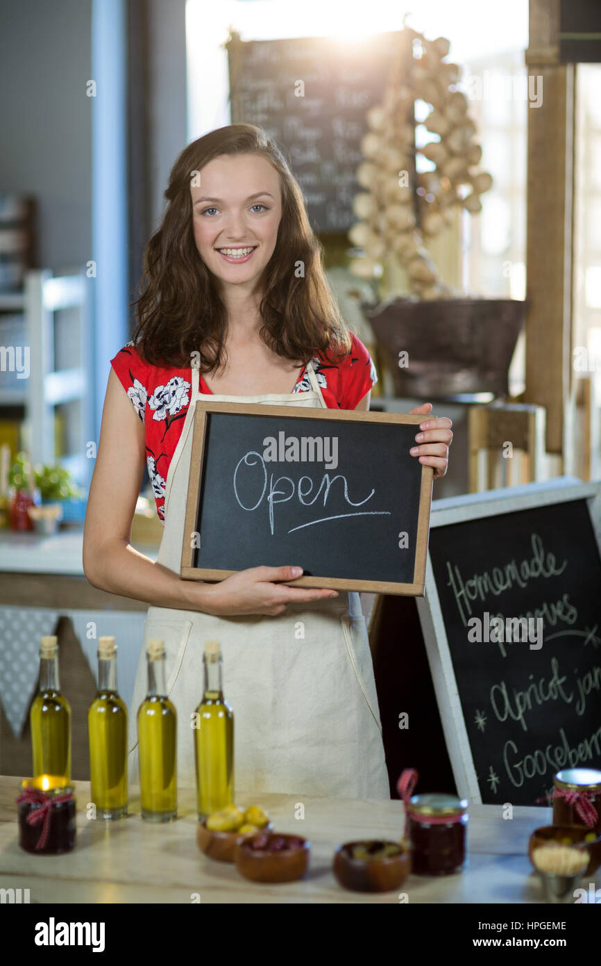 Female shop assistant holding open sign board at grocery shop Stock ...