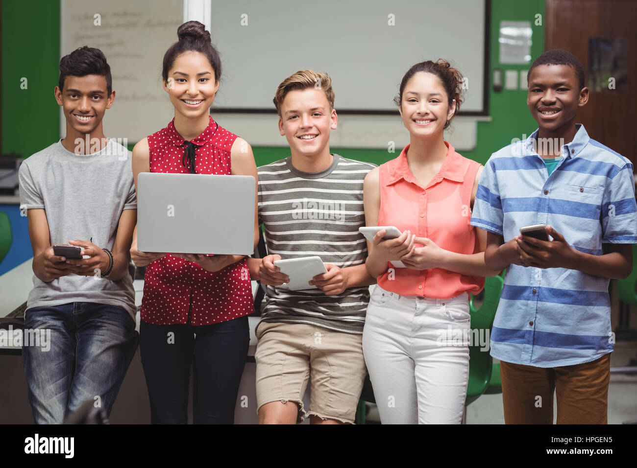 Portrait of students holding laptop, mobile phone, digital tablet in ...