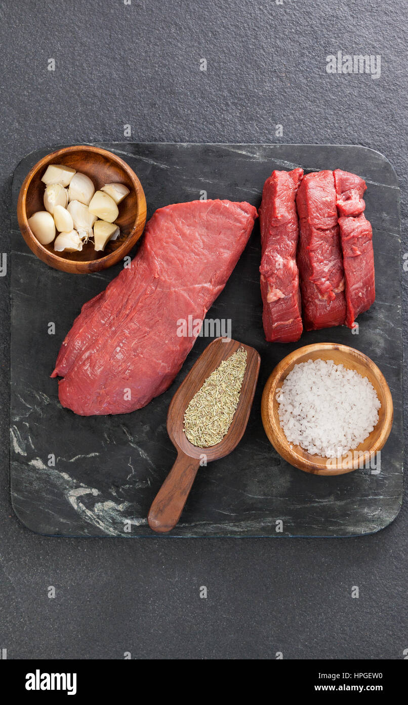 Beef steak, salt and spices on black slate plate against black ...