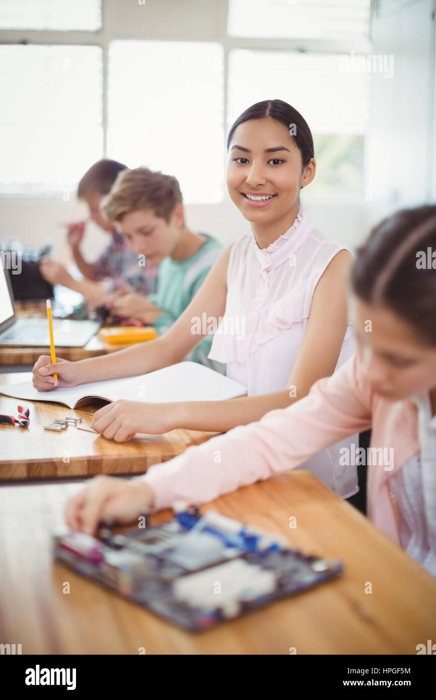 Portrait of smiling schoolgirl doing homework in classroom at school ...