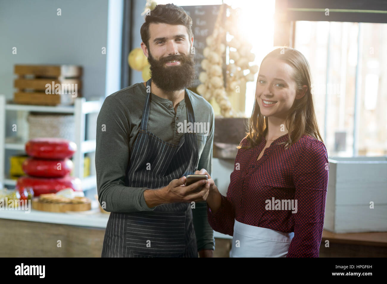 Portrait of smiling bakery staff using mobile phone at counter in bake ...