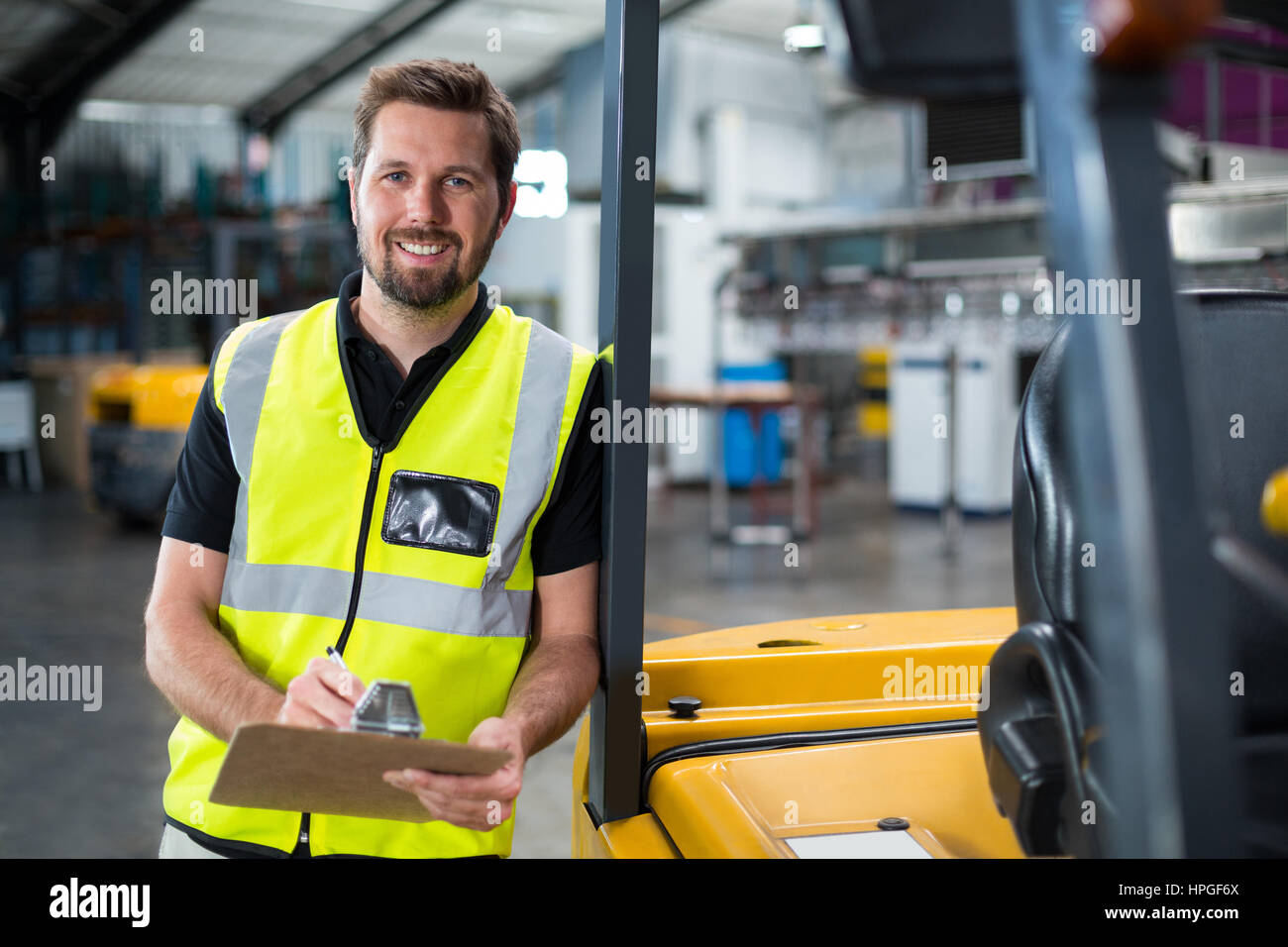 Smiling factory worker writing on clipboard in factory Stock Photo - Alamy