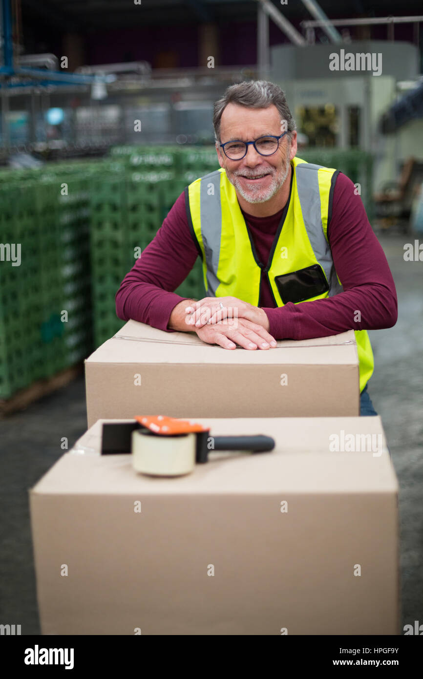 Portrait of factory worker with cardboard boxes on trolley in drinks ...
