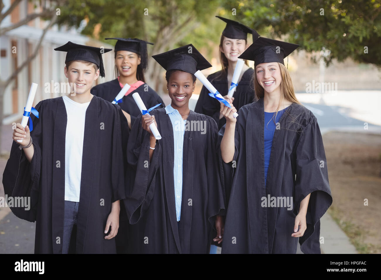 Portrait of graduate school kids standing with degree scroll in campus ...