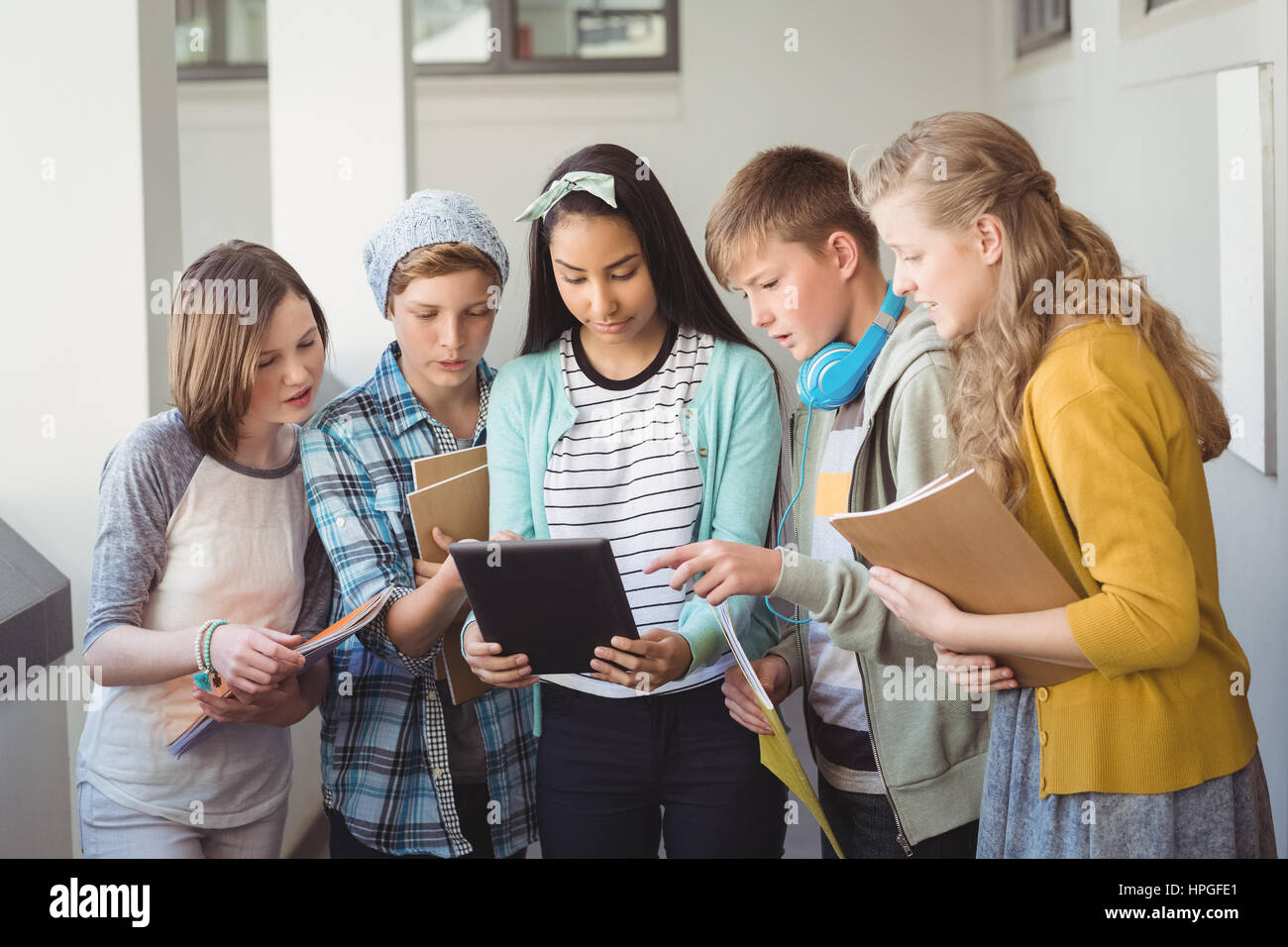 Group of school friends using digital tablet in corridor at school ...