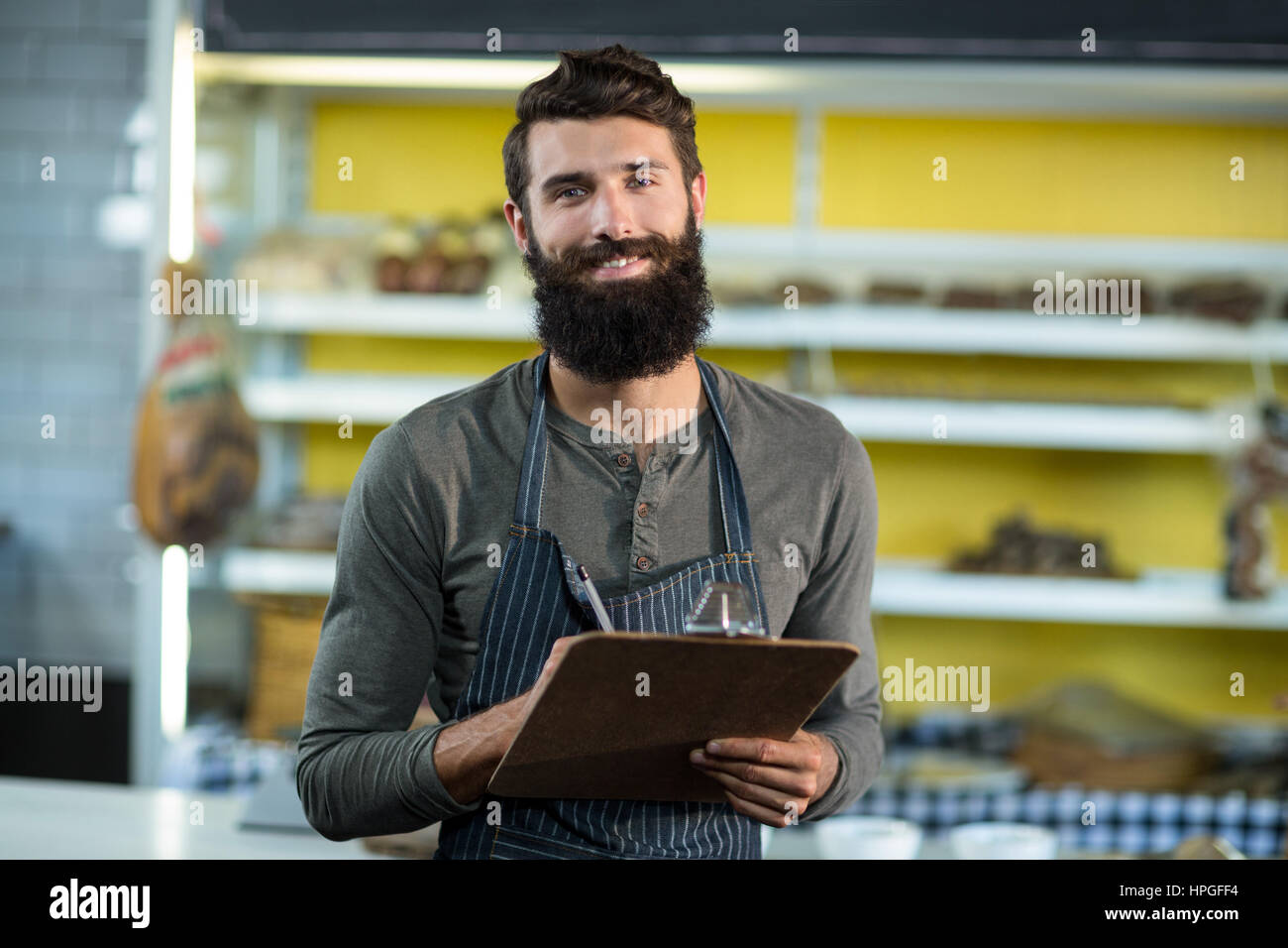 Portrait of salesman writing in clipboard at counter in grocery shop ...