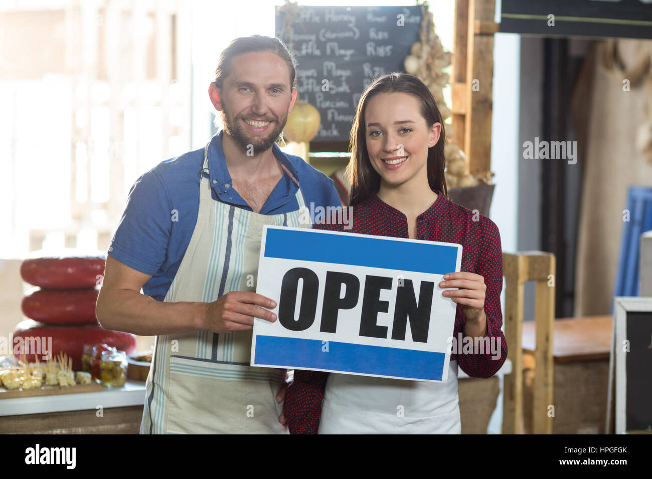 Portrait of smiling bakery staff holding board with open sign at ...