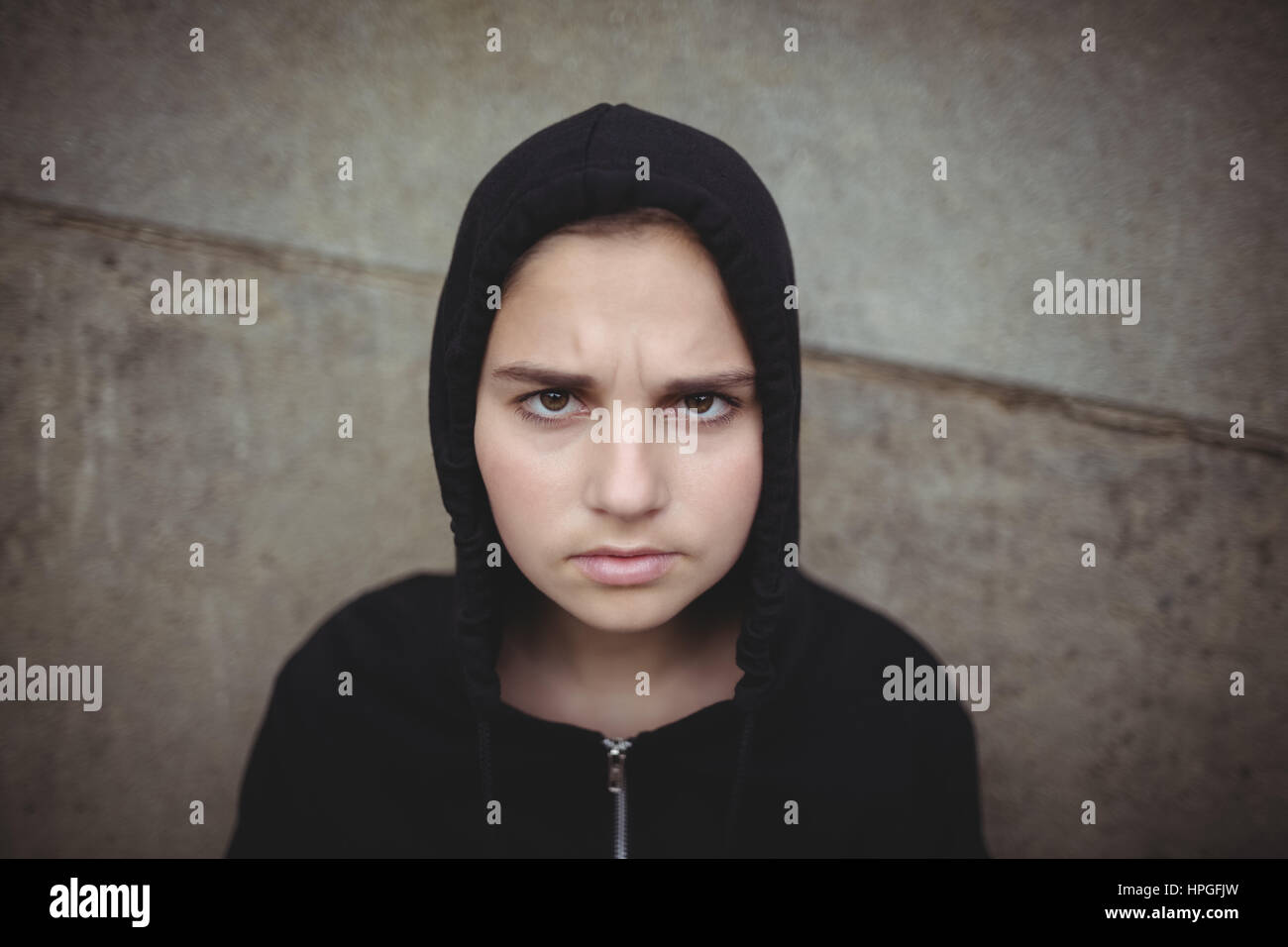 Portrait of anxious teenage girl in black hooded jacket standing at ...