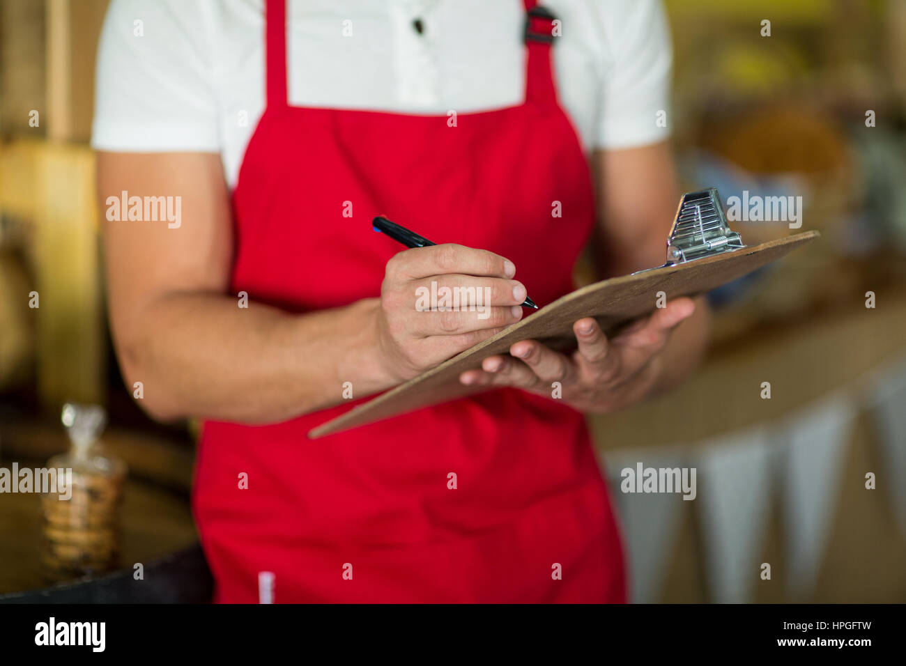 Mid section of bakery staff writing on clipboard at counter in bake ...