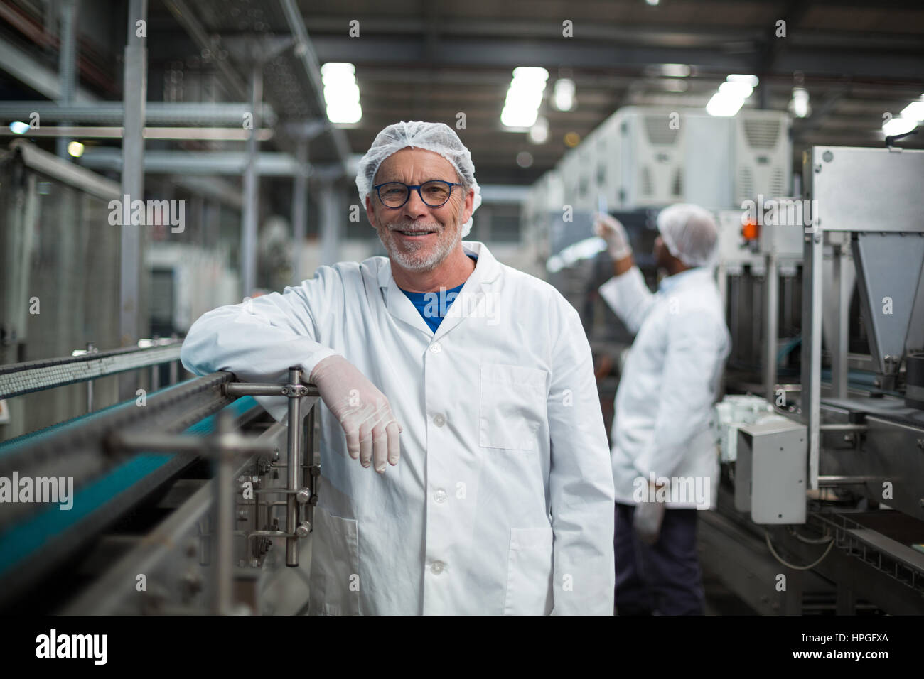 Smiling factory worker standing next to production line at drinks ...