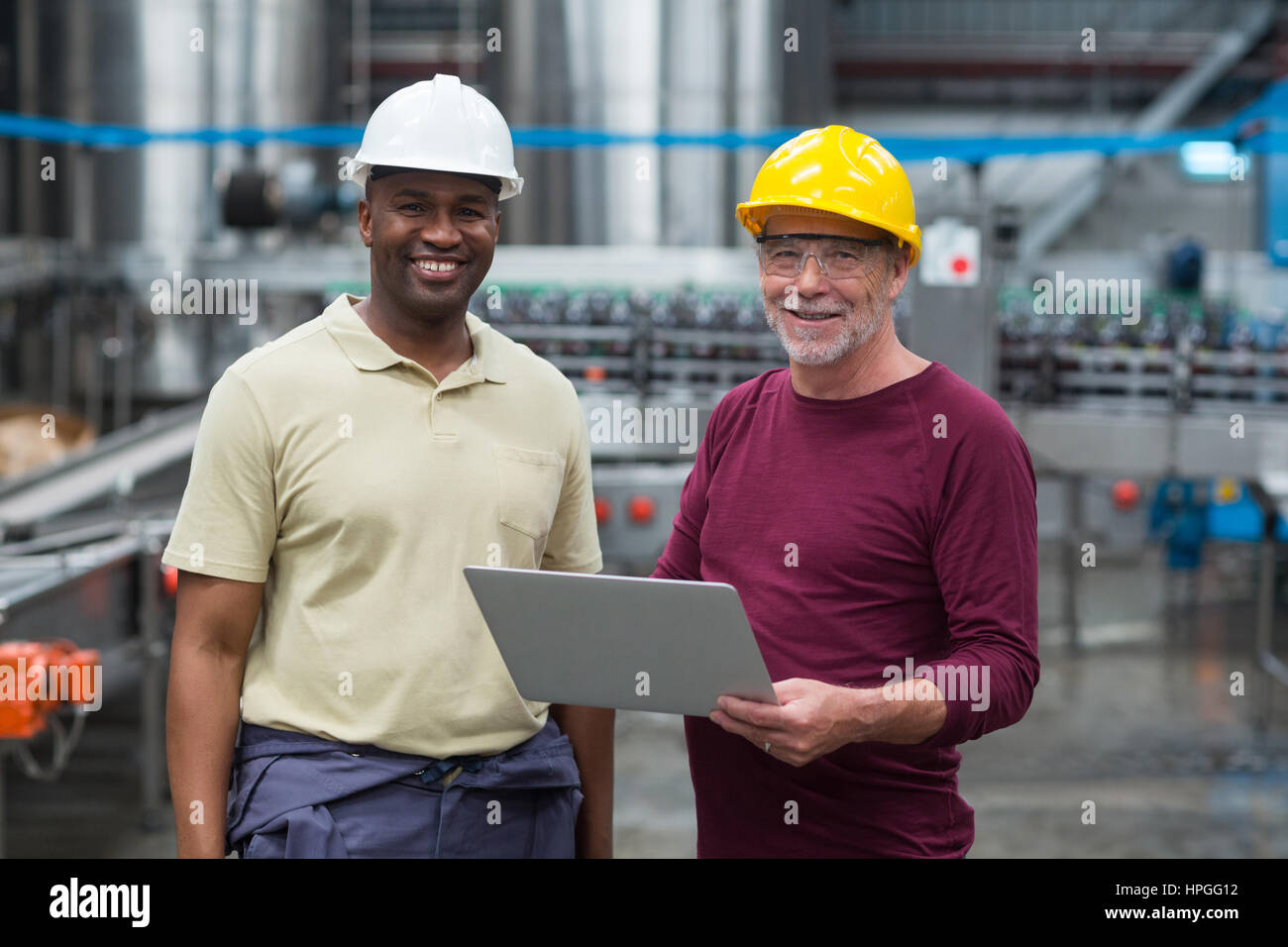 Portrait of two factory workers with laptop smiling in the drinks ...
